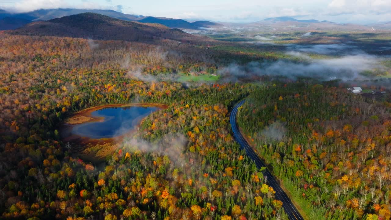 Drone footage of a lake surrounded with peak fall foliage and cloud ...