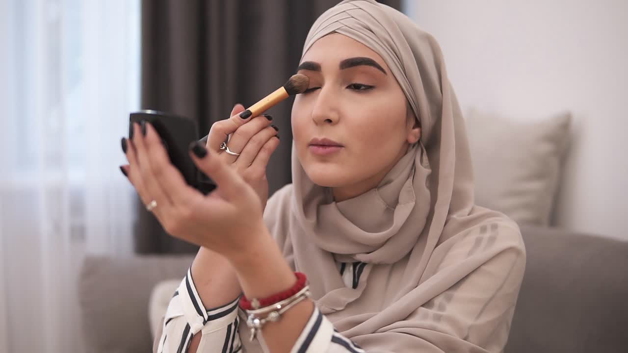 Free stock video - Muslim woman doing makeup on her face with brush