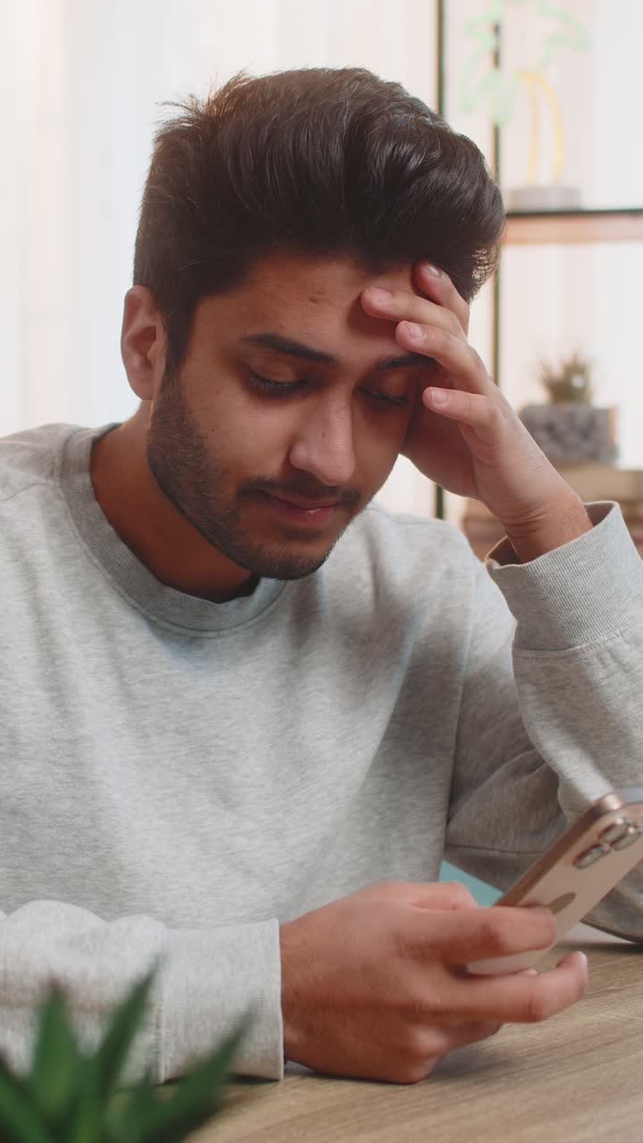 Young indian man texting on smartphone while resting head on hand at ...