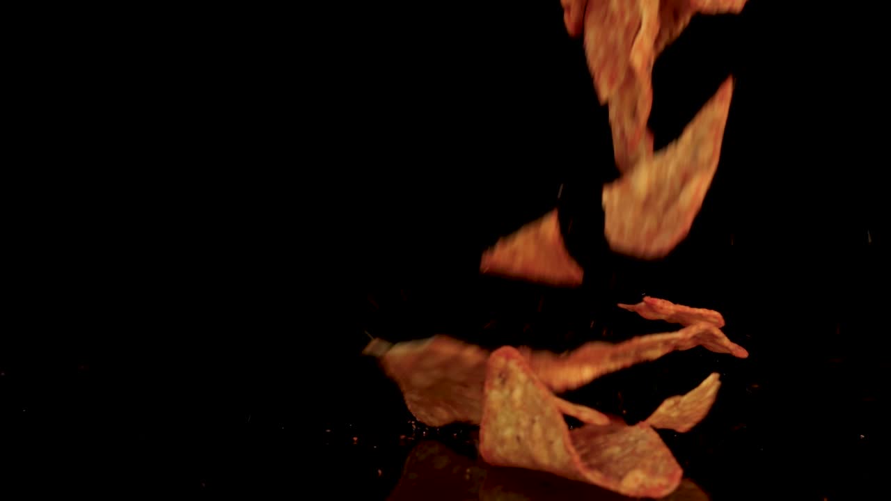 Triangular barbecue-flavored potato chips drop in slow motion onto a ...