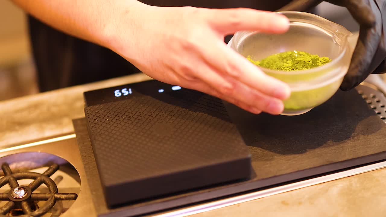 Hands carefully measure matcha powder in a glass bowl on a digital ...