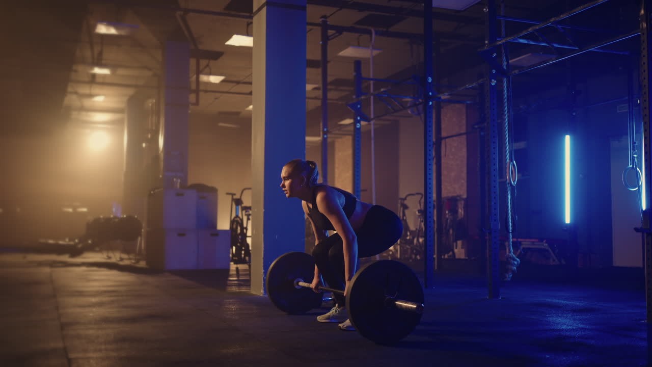 Slow motion: a woman lifts a barbell in a dark gym with a lot of weight ...