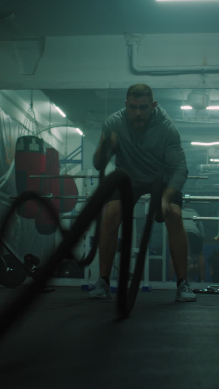 Premium stock video - Athletic man exercises with battle ropes in dark ...