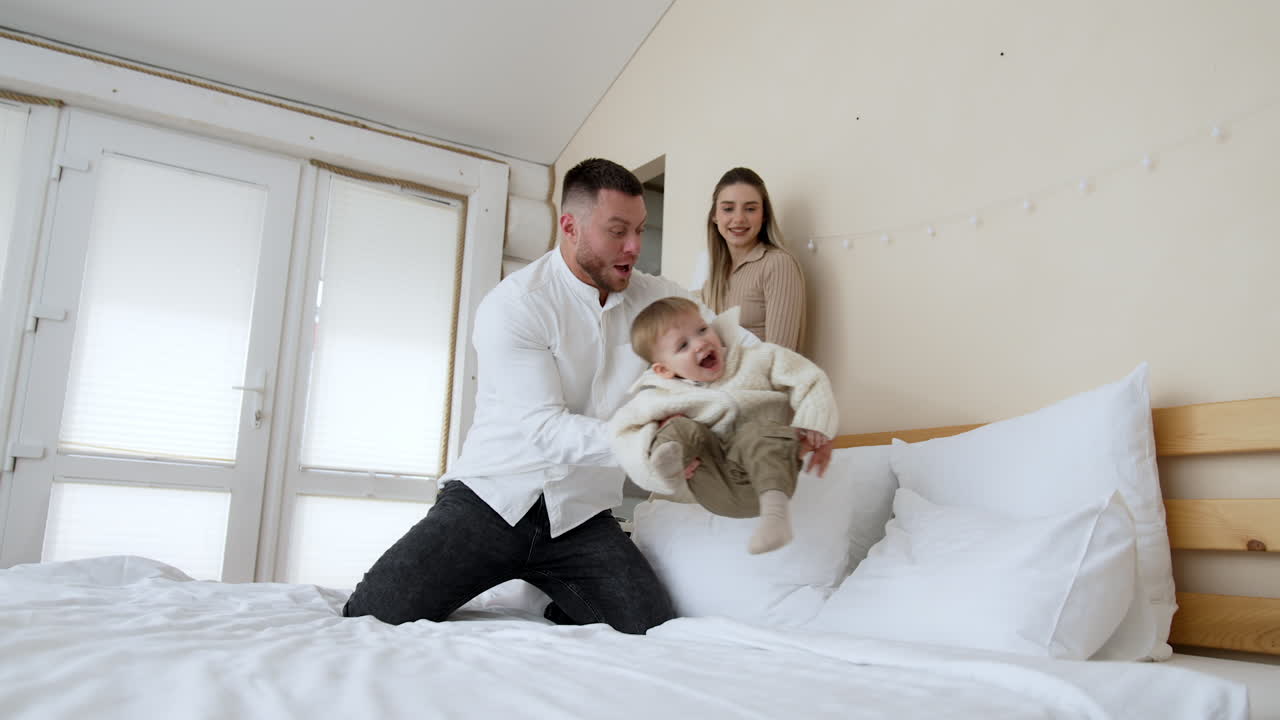 Loving Caucasian father waves his laughing baby boy on the bed. Dad ...
