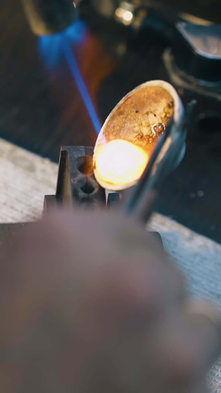CU: skilled jeweler pours molten metal into form from small crucible at ...