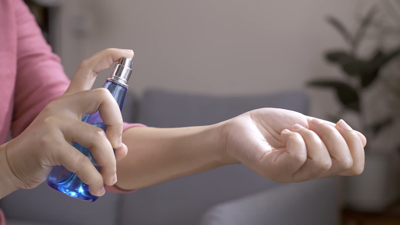 Woman spraying blue perfume on her wrist to taste the fragrance at home ...