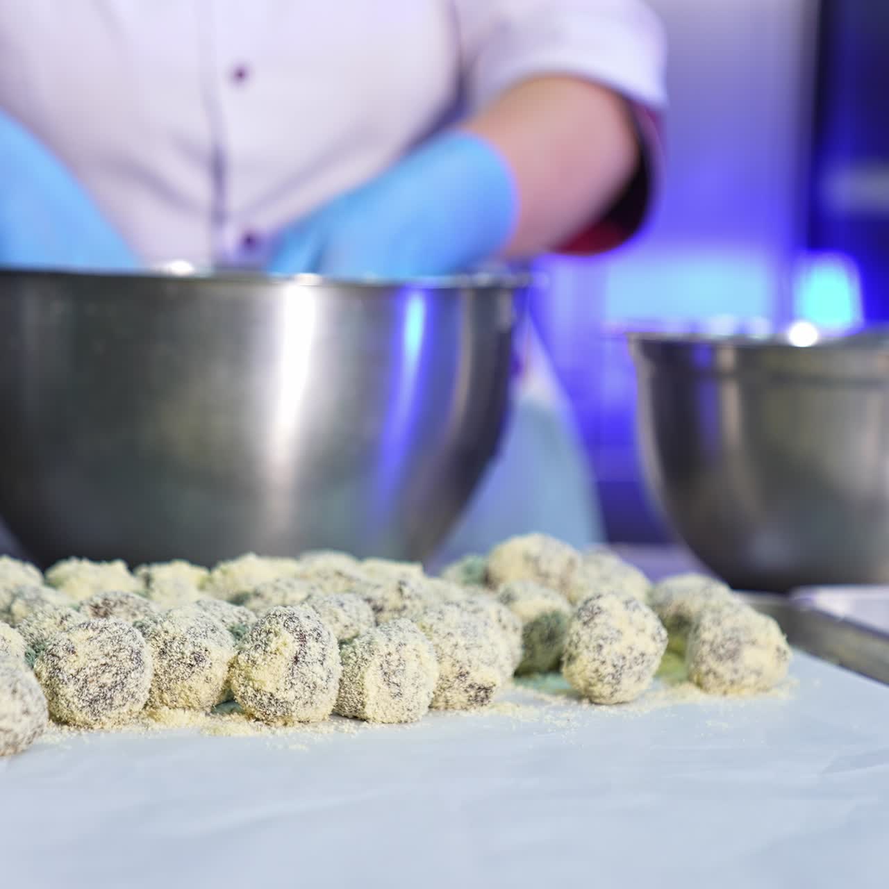 Sweet desserts in a shape of balls are laid on the tray. Worker covers ...