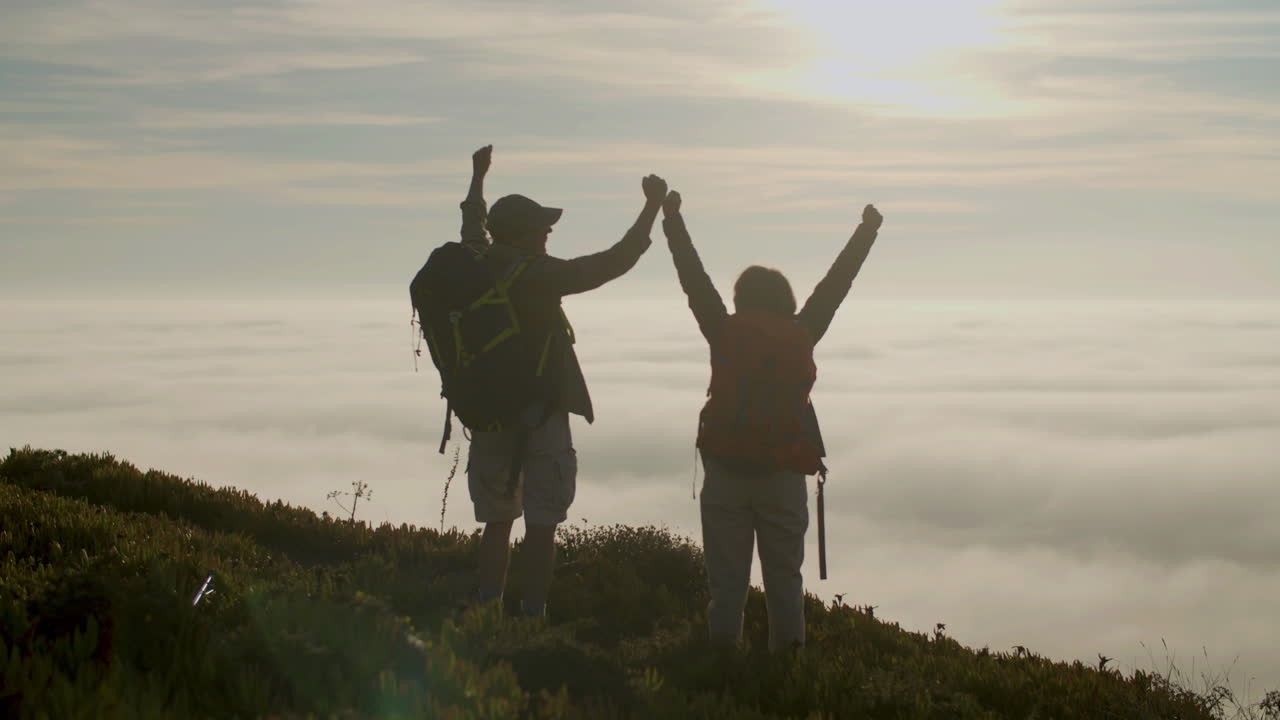 Back view of happy senior hikers raising hands while standing on the top of a mountain Free ...