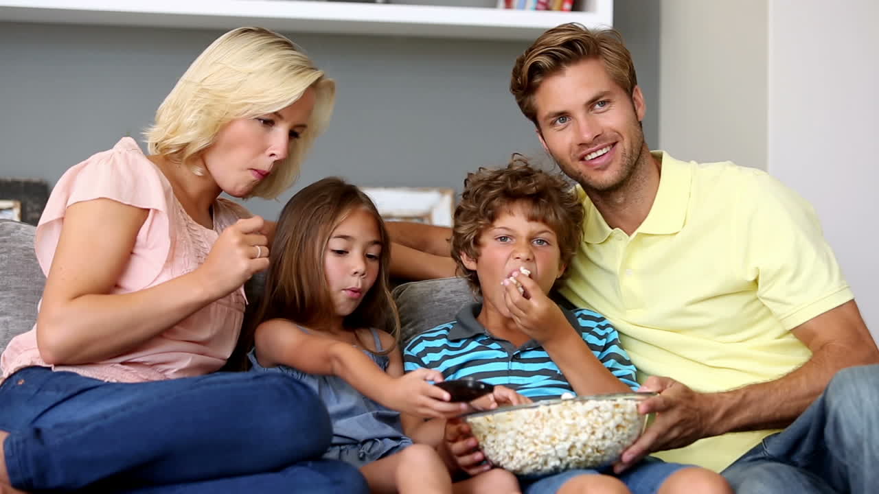 Premium stock video - Family eating popcorn and watching tv together