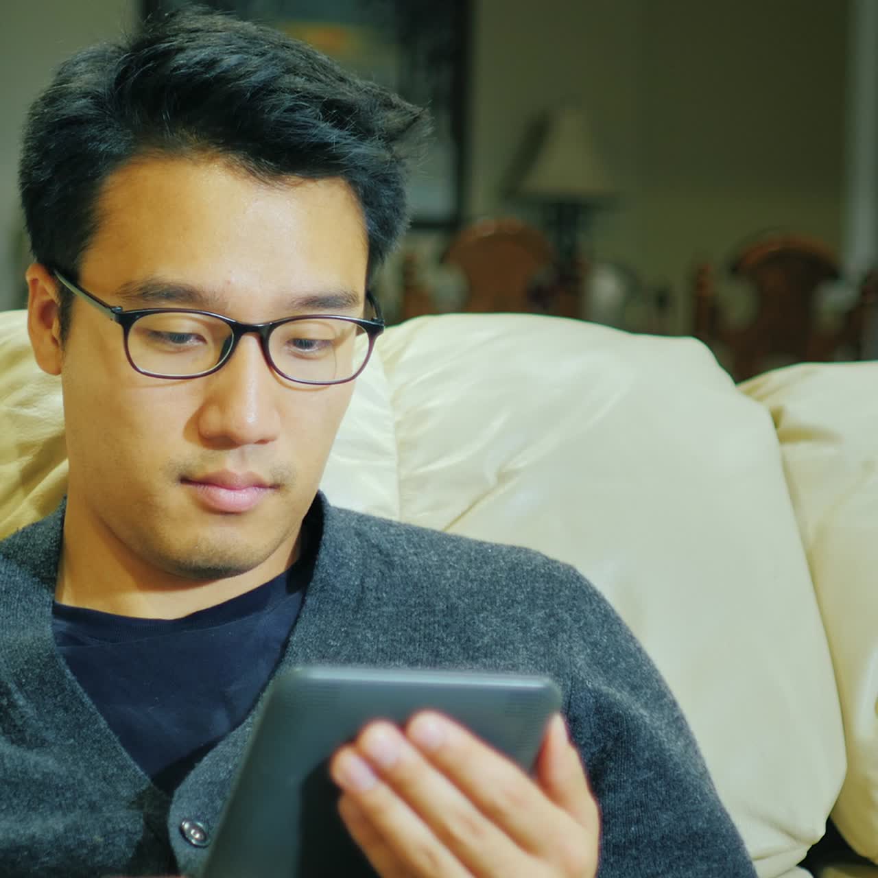 Premium stock video - A young korean man reads an e-book on the couch