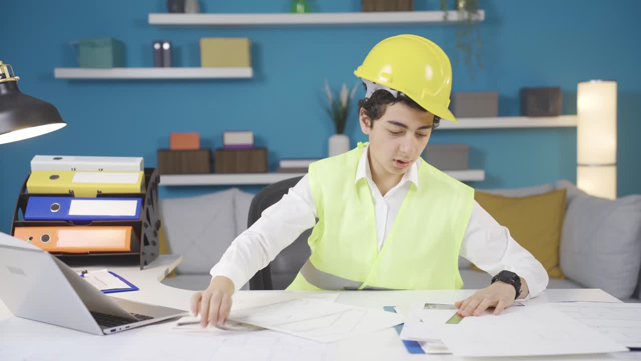 Curious boy in yellow vest and helmet sitting at table at home ...