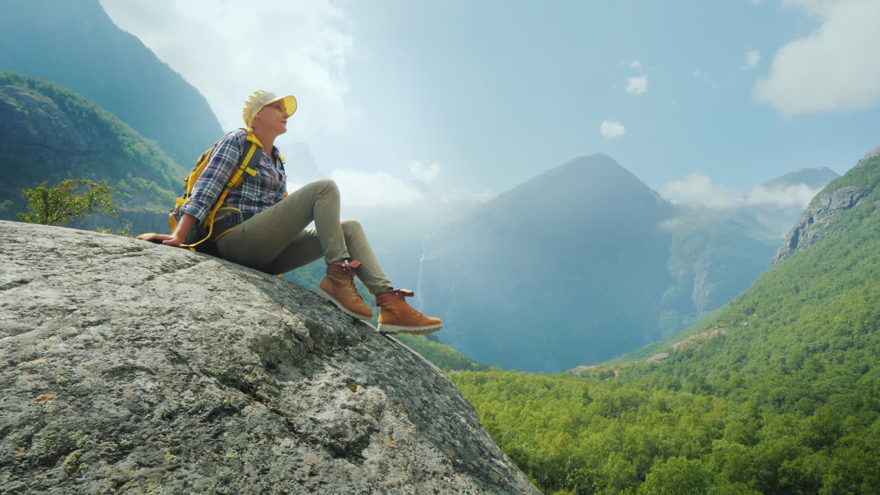 The tourist sits on a large rock surrounded by high mountains alone ...