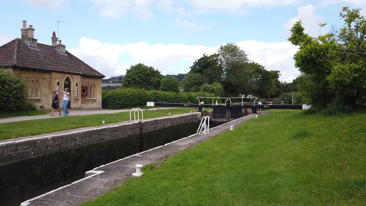 People walking alongside a canal lock and lock house on a clear day ...
