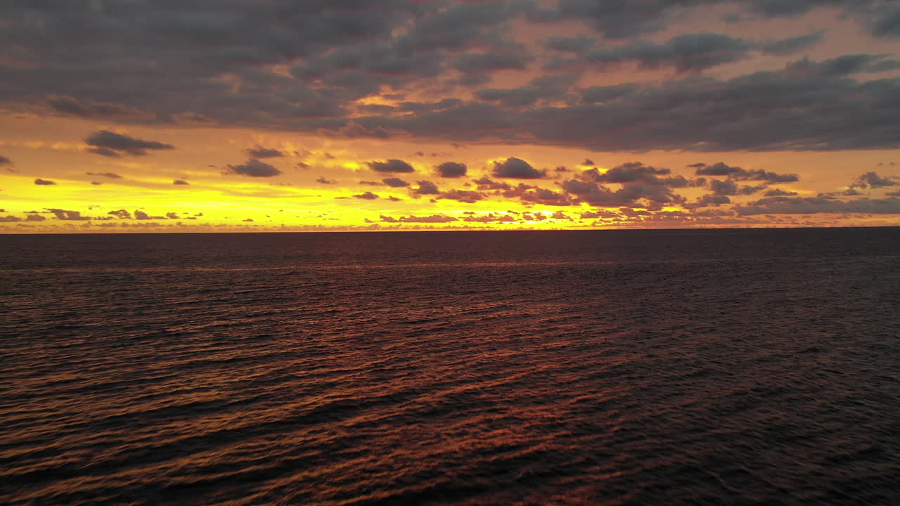 Aerial flight backwards over calm ocean with a dramatic bright yellow ...