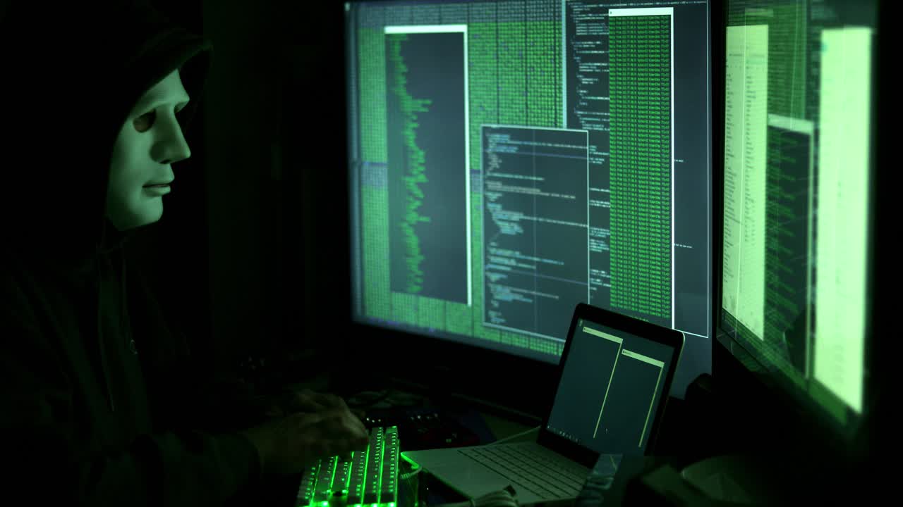 Premium stock video - Anonymous man hacking computers in dark room