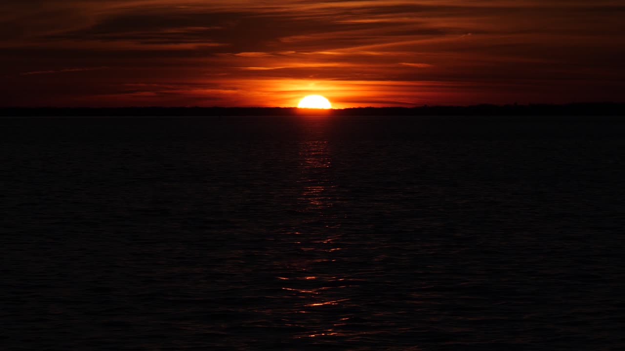Sun setting beyond dark rippling sea horizon, glowing in dim sky ...