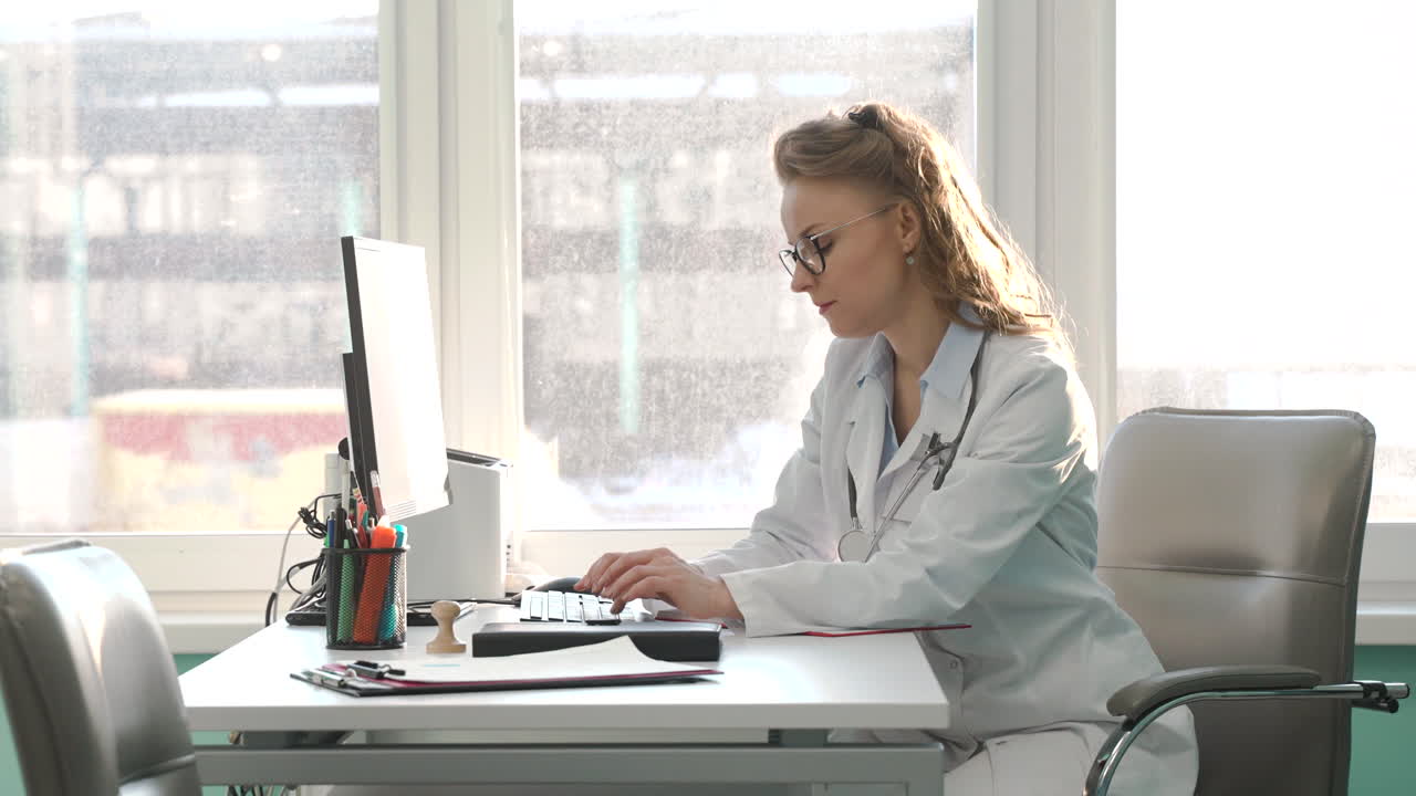 Female Doctor Working On Computer While Sitting At Desk In Her ...