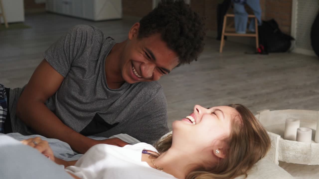 Happy multi ethnic couple lying in bed and laughing. Waking up together ...