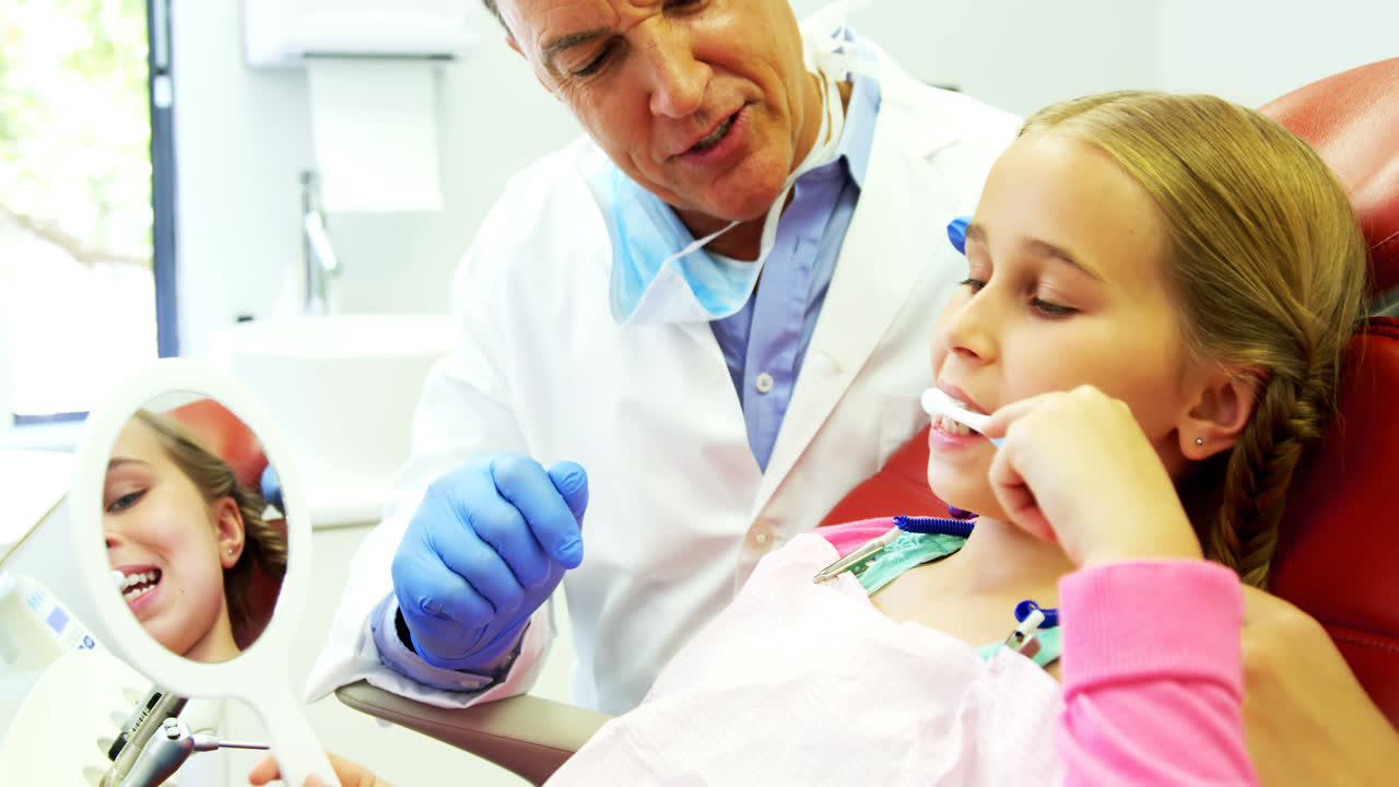Premium stock video - Dentist assisting young patient while brushing teeth