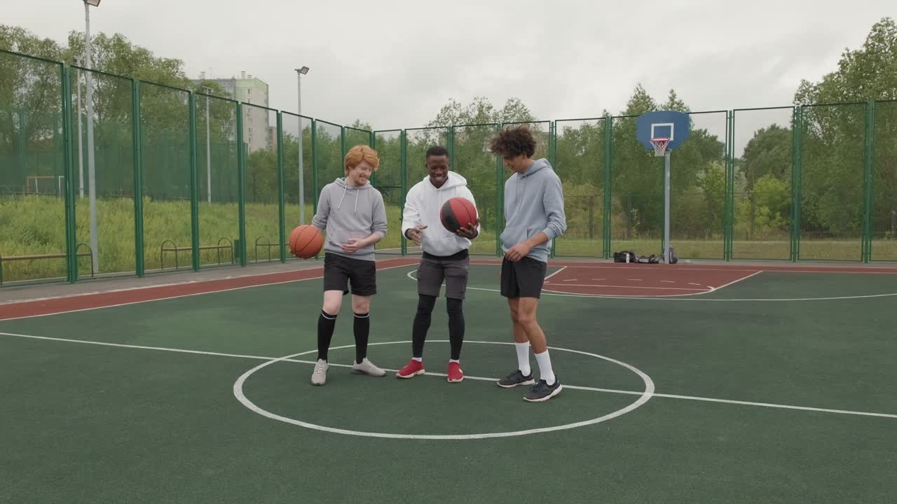 Three Friends With Basketballs On Basketball Court, Smiling And Looking ...