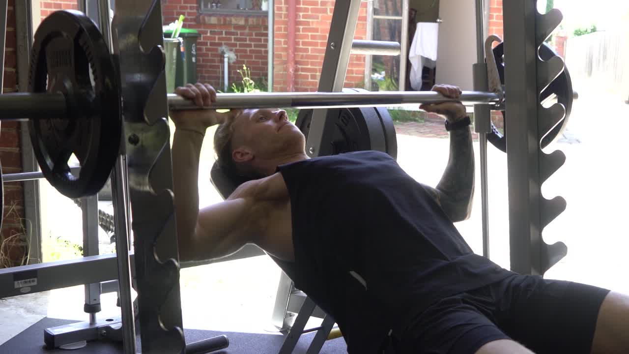 Muscly man in home gym exercising dooing incline barbell bench press ...