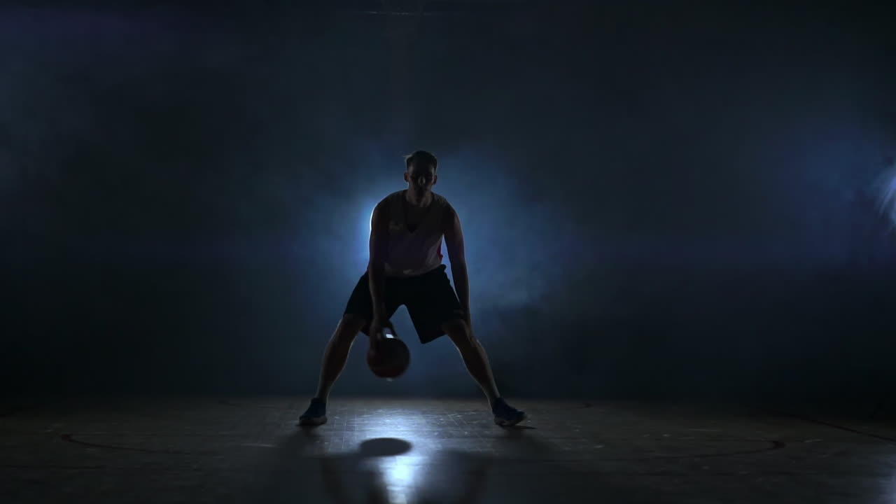 A solo basketball player does some dribbling moves in front of the ...