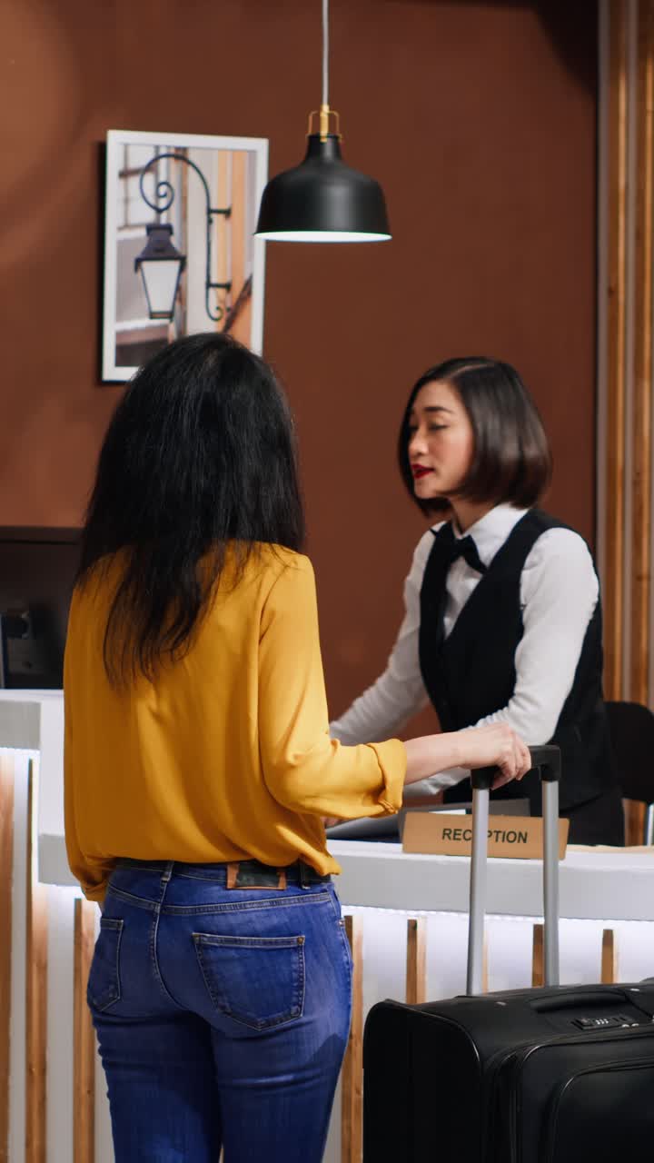 Vertical Video Asian hotel staff greeting customer at front desk ...