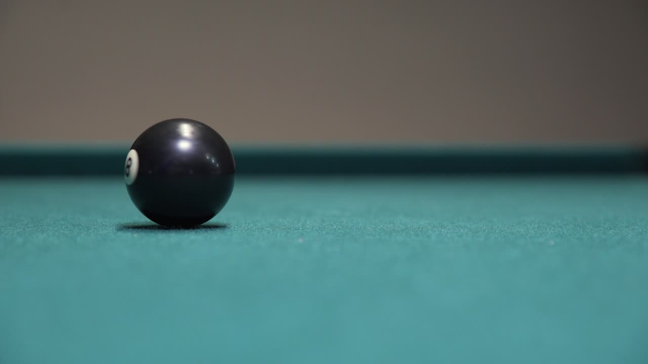 Black 8-ball spinning and rolling to a stop on a billiards table ...
