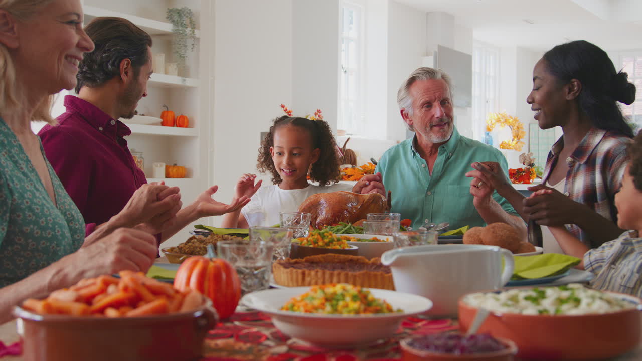 Multi-generation family celebrating thanksgiving at home saying prayer ...