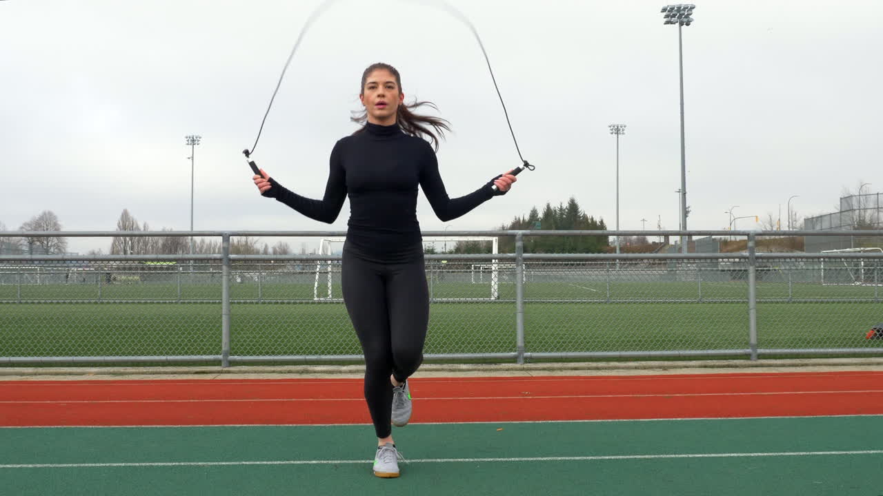 Pretty sporty girl jumping rope on cloudy outdoor track, slow motion ...