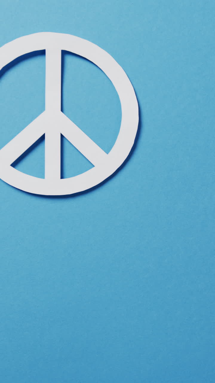 Vertical video of white peace sign and copy space on blue background ...