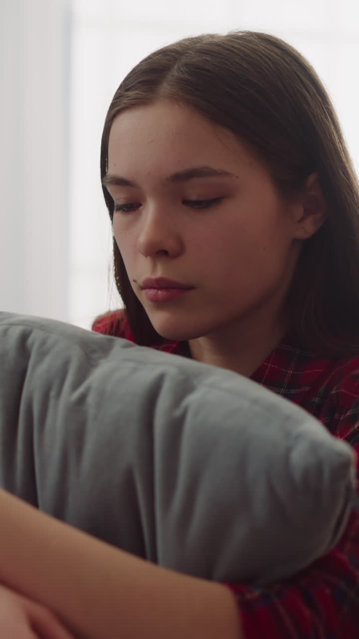 Sad young woman sits hugging pillow on couch in living room zoom in ...