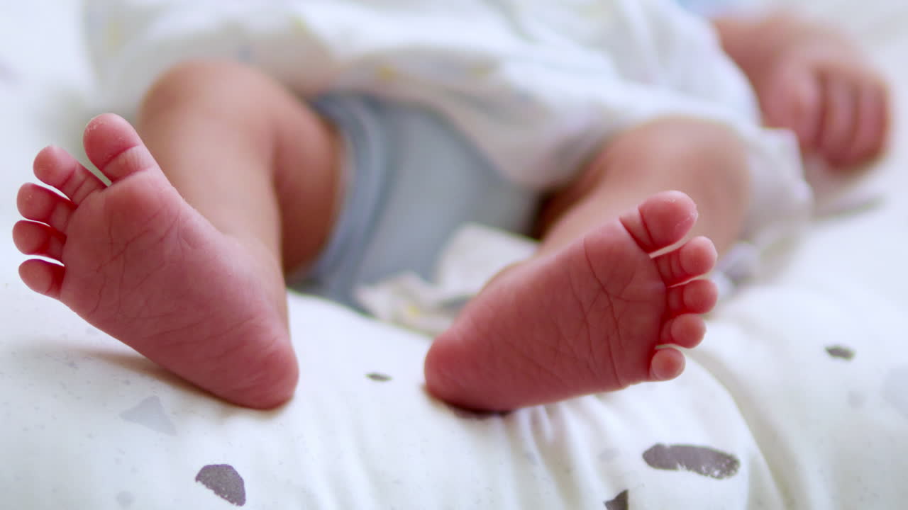 Close-up shot of the cute, tiny feet and toes of a newborn baby as she ...