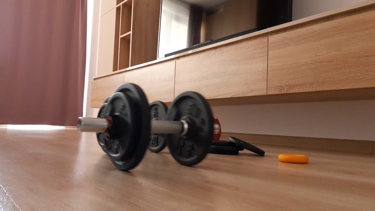 Premium stock video - Dumbbells roll on the floor in the living room