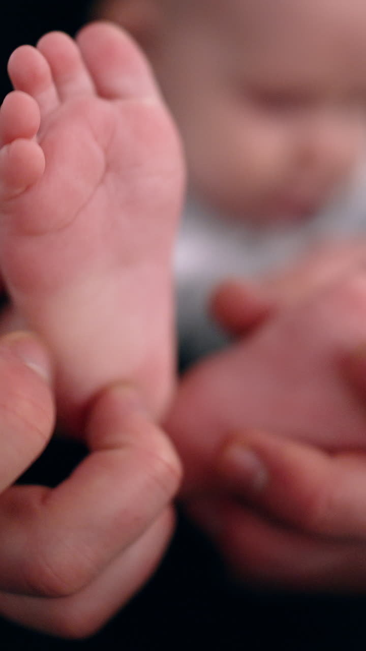 Dad's hands hold the tiny feet of his baby. Father tickles and claps ...