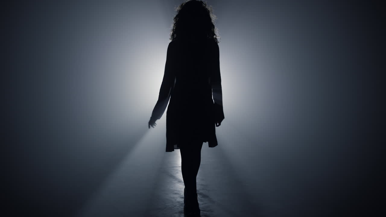 Silhouette woman walking in darkness. Girl walking in floodlight ...