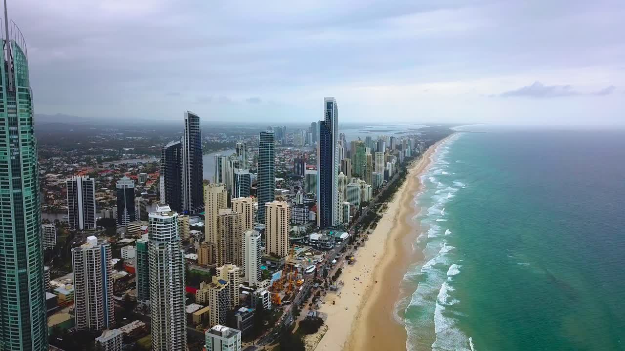 Aerial moving back view of skyscraper city by the beach with turquoise ...