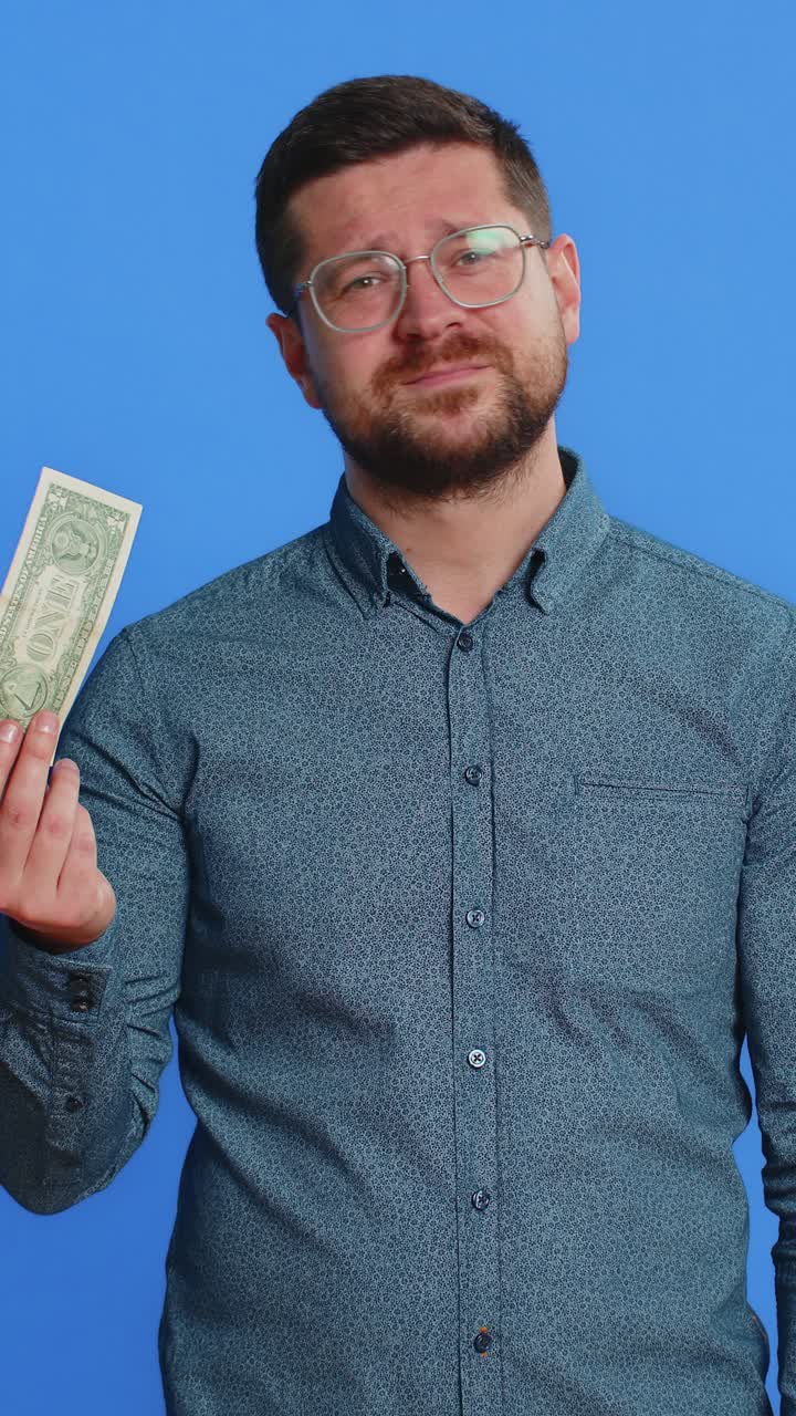Poor man in glasses insufficient amount of money holding one dollar ...