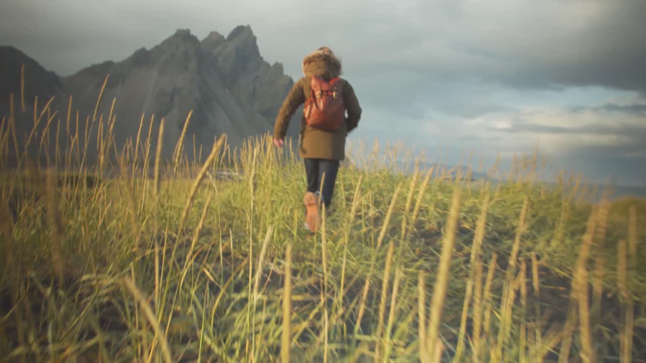 Hiker running through grassy dunes on a beach in front of a rocky ...